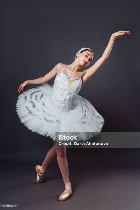 백조 호수에서 백조의 투투 스커트에 젊은 아름다운 우아한 백인 발레리나 연습 발레 위치의 초상화 발가락에 서있는 회색 배경에