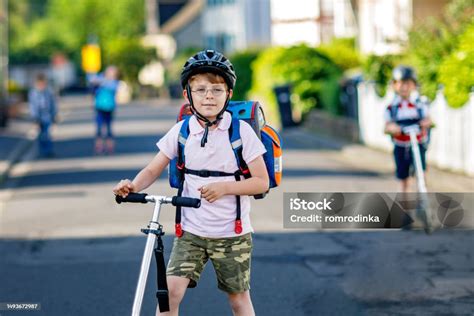 화창한 날에 배낭을 메고 도시에서 스쿠터를 타고 안전 헬멧을 쓴 두 명의 학교 소년 화려한 옷을 입은 행복한 아이들이 학교에 가는 길에 자전거를 타고 있다 야외에서 아이들이