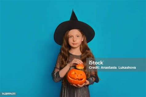 마녀 의상을 입은 귀여운 아이 소녀는 할로윈 호박이나 잭 오 랜턴 호박 꼭대기를 들고 파란색 배경으로 카메라를 바라 봅니다 8 9 살에 대한 스톡 사진 및 기타 이미지
