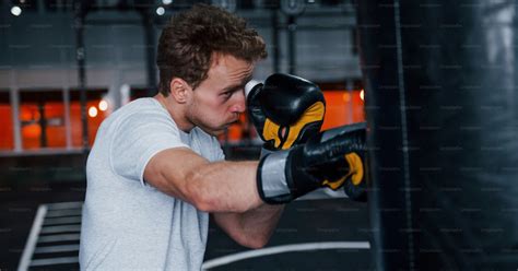 흰 셔츠와 권투 보호 장갑을 낀 청년이 가방을 밀고 체육관에서 운동을 하고 있다 사진 Unsplash의 스포츠 이미지