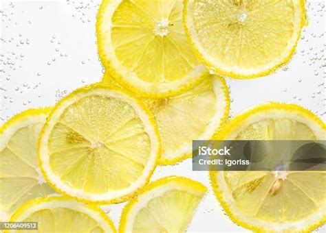 Стокове фото Скибочки Лимона У Воді З Бульбашками Повітря На Білому — Завантажте зображення