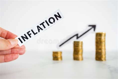 Hand Holding Inflation Text In Front Of Growing Stacks Of Coins With Arrow Going Up In The