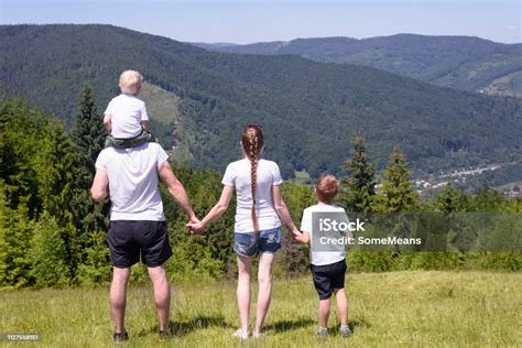 아버지 어머니 및 2 명의 작은 아들은 나무가 우거진된 언덕의 배경에 녹색 필드에 서 있다 가족의 가치 2명에 대한 스톡 사진 및 기타 이미지 Istock