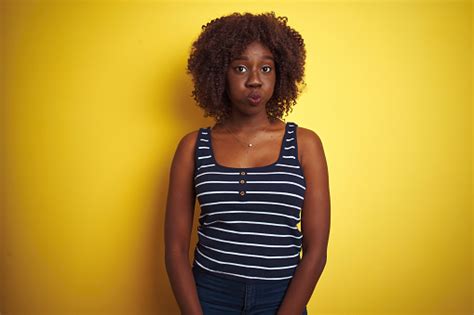 젊은 아프리카 아프로 여자 는 재미있는 얼굴과 고립 된 노란색 배경 퍼핑 뺨 위에 줄무늬 티셔츠를 입고 공기 미친 표정으로 입이 팽창 T 셔츠에 대한 스톡 사진 및 기타