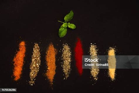 검은 배경에 흩어져있는 향신료 고수풀 마요라나 파프리카 백리향 및 로즈마리 보편적 조미료 마늘민트 잎 옆에 어두운 배경에 쌓여 있습니다 가루로 빻은에 대한 스톡 사진 및
