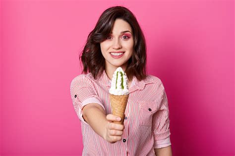 아이스크림을 제공 하는 즐거운 찾고 여자의 초상화를 닫습니다 레이디를 입고 줄무늬 셔츠 스탠드 분홍색 배경에 고립 된 미소 여자는 맛 있는 콘을 들고 광고를 위한 공간을