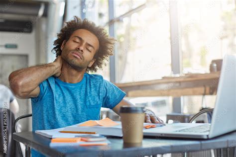 Young Tired Manager Sitting In Restaurant Surrounded With Papers And Laptop Computer Having