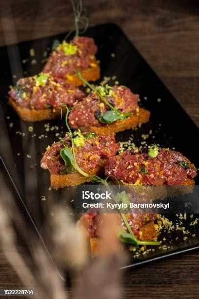 마이크로그린과 아보카도 한 조각으로 장식된 비프 타르타르에 마늘 버터에 볶은 구운 메밀 빵을 얹은 요리 음식은 나무 배경에 직사각형 세라믹 접시 위에 놓여 있습니다 0명에