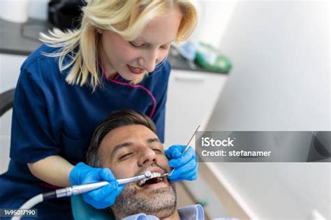 젊은 여성 치과의사가 치과에 진료를 하는 동안 환자의 치아를 검사하고 있다 환자의 입 근처에 치과 기구를 들고 있는 의사의 손 건강한 치아와 의학 개념 2명에 대한 스톡