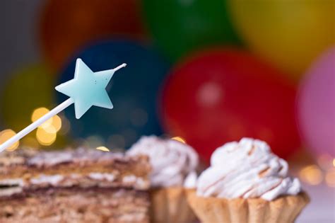 여러 가지 색상의 풍선과 조명의 배경에 파란색 별 모양의 촛불이있는 축제 컵 케이크 파티 생일 개념 공간을 복사합니다 고독