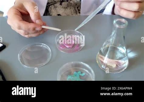Unrecognizable Female Scientist Pouring Liquid From Pipette Over Pink Glitter Sample On A Petri