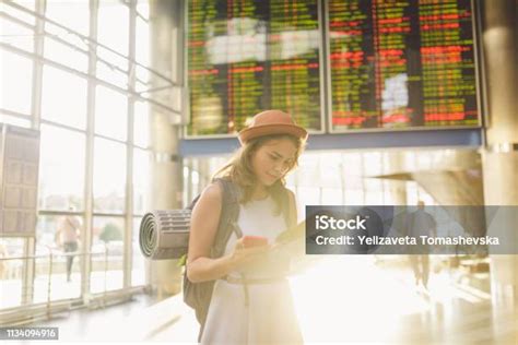 테마 여행과 교통 기차 역 터미널 내부에 서 있는 아름 다운 젊은 백인 여자 드레스와 배낭 전화를 들고 전자 득점판을 보고 지도 종이 손 항법 가리기에 대한 스톡 사진 및