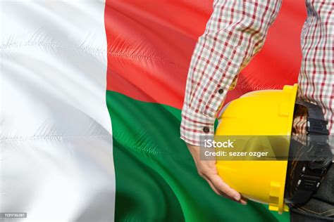 Malagasy 엔지니어는 마다가스카르 국기 배경을 흔들며 노란색 안전 헬멧을 들고 있다 건축 및 건축 개념 개념에 대한 스톡 사진 및 기타 이미지 Istock