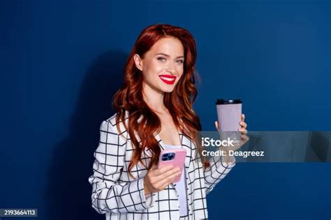 눈에 띄는 빨간 머리와 강렬한 립스틱을 바른 젊은 여성이 짙은 파란색 배경에 커피잔과 스마트폰을 들고 있습니다 20 24세에 대한 스톡 사진 및 기타 이미지 Istock