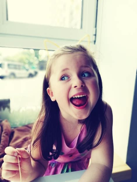 Premium Photo Cute Girl With Mouth Open Sitting Against Window At Home