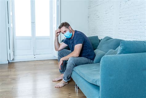 코로나바이러스 사망 직장 분실 잠금 및 사회적 불변으로 인해 피곤하고 걱정스러운 고통을 느끼는 집 거실 소파에서 보호 얼굴 마스크를 쓴 슬픈 남자 정신 건강과 격리 개념