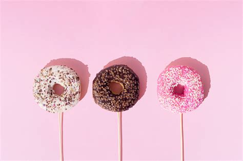 화이트 핑크 초콜릿 유약과 함께 링 도넛을 배열 롤리팝과 같은 나무 막대기에 분홍색 파스텔 배경에 화려한 부스러기 무늬 공간을 복사합니다 플랫 레이 롤리팝에 대한 스톡 사진