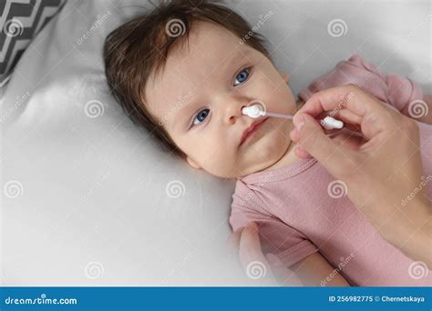 Mother Cleaning Nose Of Her Baby With Cotton Bud On Bed Top View Stock
