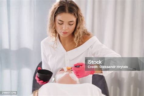 스킨케어 전문가가 클레이 마스크를 고객의 얼굴에 철저하게 펴 바르고 균형 잡힌 안색을 위해 균일한 커버력을 보장합니다 2명에 대한 스톡 사진 및 기타 이미지 Istock