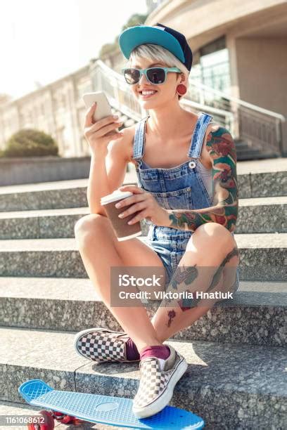 스케이트 보드 모자와 선글라스에 앉아 다른 여자 스케이터 뜨거운 커피 브라우징 스마트 폰 쾌활한 와 페니 보드에 계단 발에 앉아 스마트폰에 대한 스톡 사진 및 기타 이미지