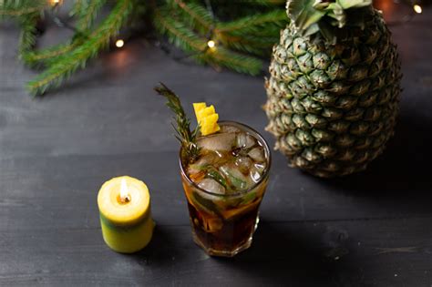 파인애플 럼주 콜라 얼음 민트 로즈마리를 연 크리스마스와 새해 칵테일로 불타는 촛불 신선한 과일 장식 된 전나무 나무 가지와 함께 검은 나무 배경에 유리로 로즈마리 건강한