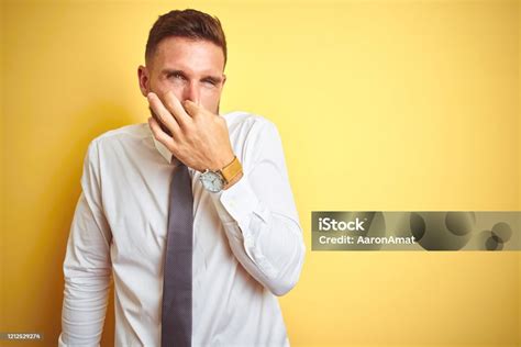 노란색 고립 된 배경 위에 우아한 흰색 셔츠를 입고 젊은 잘 생긴 사업가 뭔가 냄새와 역겨운 참을 수없는 냄새 코에 손가락으로 숨을 들고 나쁜 냄새 개념 경영자에 대한 스톡