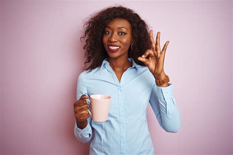 젊은 아프리카 계 미국인 여자 마시는 컵 의 커피 위에 고립 된 분홍색 배경 하 고 확인 기호 와 손가락 우수한 기호 개념에