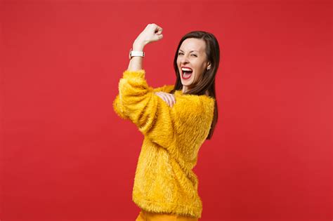 이 두 근을 보여주는 노란 모피 스웨터에 강한 재미 젊은 여자의 측면 보기 스튜디오에서 밝은 붉은 벽 배경에 고립 된 근육 사람들은 진심으로 감정 라이프 스타일 개념입니다