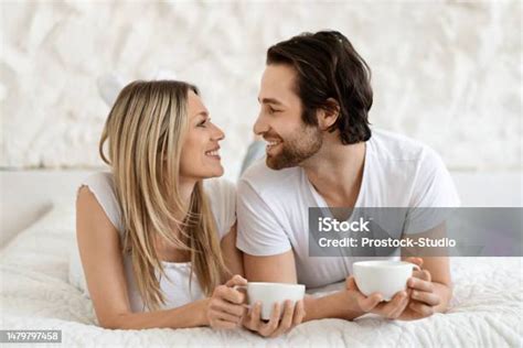 침대에서 아침 음료 행복한 사랑하는 아내와 남편은 뜨거운 커피 한 잔과 함께 하얀 침대에 누워 서로를 바라보고 있다 20 24세에 대한 스톡 사진 및 기타 이미지 Istock