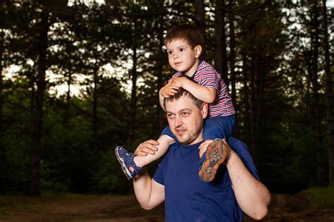 아빠는 아들을 어깨에 짊어지며 목을 감고 다닙니다 아버지와 아들은 저녁에 나무 들 사이 야생숲에서 산책 사랑과 가족 2 3 살에