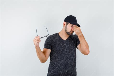 Free Photo Young Man Taking Off Glasses Massaging Eyes In T Shirt And Cap And Looking Fatigued