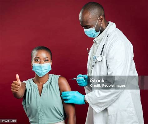 아프리카 계 미국인 코비드 예방 접종을받은 여성은 엄지 손가락으로 기호와 기호를 보여줍니다 흑인 의사가 외과 용 안면 마스크를 착용 한 환자에게 백신을 제공합니다