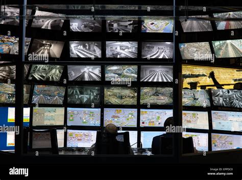 Security Monitoring Control Console Room With A Wall Of Screens And Two