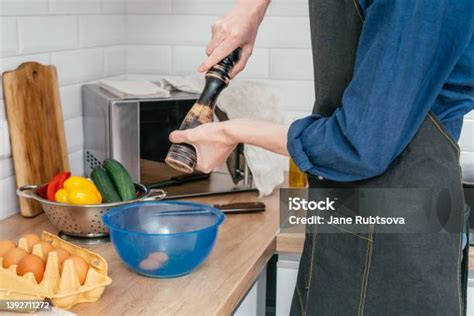 소쿠리 근처의 테이블에 파란색 플라스틱 그릇에 나무 향신료 분쇄기로 두 개의 달걀을 후추 칠하는 인식 할 수없는 남자의 측면보기 가정 생활에 대한 스톡 사진 및 기타 이미지