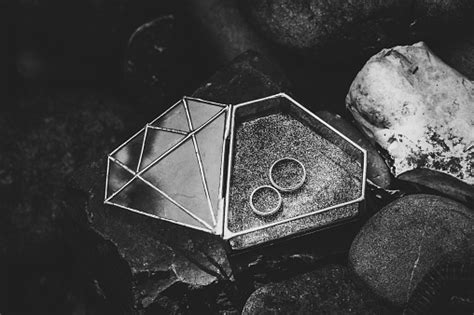 웨딩 골드 실버 약혼 반지는 다이아몬드 모양의 유리 모양의 금속 상자에 거짓말 둥근 큰 돌의 배경에 화려한 파란색 표면에 결혼 반지 닫 다 결혼 의식에 대한 스톡 사진 및