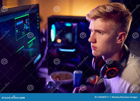 Male Teenage Hacker Sitting In Front Of Computer Screens Bypassing Cyber Security Stock Image