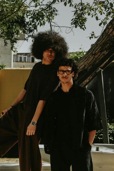 집 밖의 갈색 바지 거리 스타일 거리 패션 검은 셔츠 곱슬머리 관찰 나무 남성 모델 남성 패션 녹색 단풍 도시 배경 도시 생활 도시 패션 도시