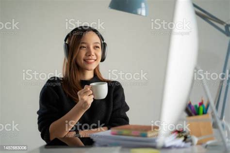 젊은 자신감 넘치는 아시아 사업가가 커피 한 잔을 들고 사무실 책상에 앉아 노트북 컴퓨터로 작업하고 있다 경영자에 대한 스톡 사진 및 기타 이미지 Istock