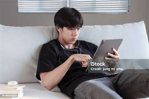 매력적이고 진지한 젊은 대학생 남자가 거실 소파에 앉아 디지털 태블릿을 사용하여 메일을 확인하는 초상화 20 24세에 대한 스톡 사진 및 기타 이미지 Istock