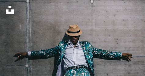 회색 벽 근처에 서 있는 검은 모자를 쓰고 녹색과 흰색 꽃무늬 긴팔 드레스를 입은 여자 사진 Unsplash의 무료 스타일 이미지