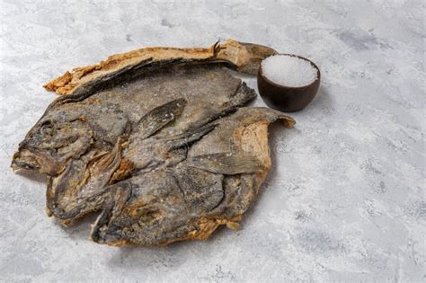 Salted Dry Raw Cod On A Light Textured Background With A Well Of Salt