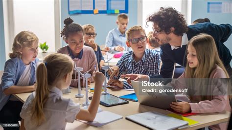 초등학교 교실 태블릿 컴퓨터를 들고 열정적인 교사가 풍력 터빈이 어떻게 작동하는지 훌륭한 어린 아이들에게 설명합니다 재생 에너지의 친환경 형태에 대해 배우는 아이들 초등