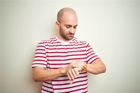 젊은 대머리 남자 수염 을 입고 캐주얼 스트라이프 레드 티셔츠 위에 흰색 고립 된 배경 손목 시계에 시간을 확인 편안하고 자신감