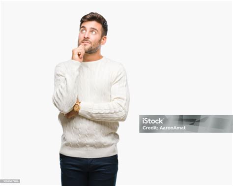 잘생긴 젊은이 손으로 턱 질문 잠겨있는 표현에 대 한 생각에 고립 된 배경 위에 겨울 스웨터를 입고 사려깊은 얼굴 미소 의심