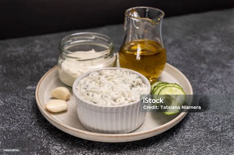 전통적인 그리스 요구르트 소스 Tzatziki 흰 그릇에 드레싱 강판 오이 사워 크림 요구르트 올리브 오일 마늘 짙은 회색 콘크리트 테이블에 재료를 넣은 허브 가로 강판에
