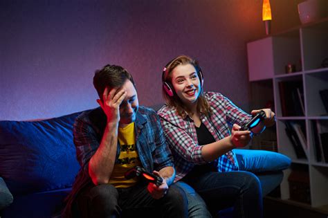 미친 장난 커플의 초상화 소파에 앉아 실내 플레이 스테이션에서 비디오 게임을 즐기는 게이머 손에 콘솔 게임 패드를 들고 X 박스