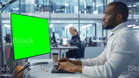 다양한 현대 사무실 녹색 화면 모의 디스플레이와 데스크톱 컴퓨터를 사용하여 잘 생긴 흑인 사업가 전자 상거래 앱 개발 프로젝트