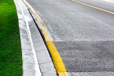 운하에 빗물을 흐르는 것은 흐린 날에 비가 내린 후 노란색 표시가있는 아스팔트 도로 의 측면에있는 배수 시스템의 시멘트 도랑과 녹색 잔디입니다 0명에 대한 스톡 사진 및