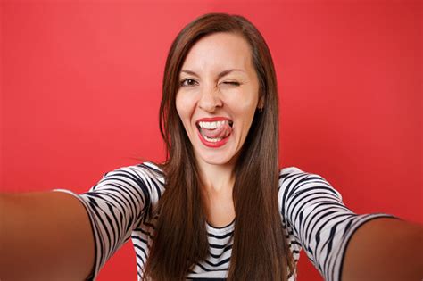 점멸 밝은 빨간 벽 배경에 고립 된 혀를 보여주는 캐주얼 스트라이프 옷에 쾌활 한 젊은 여자의 Selfie 총 닫습니다 사람들이 진심으 감정 라이프 스타일 개념 복사 공간을