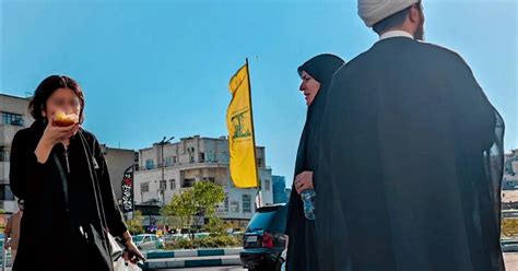 زیر پرچم حزب‌الله و کنار یک آخوند؛ حضور شجاعانه زن جوان بدون حجاب اجباری ایران اینترنشنال